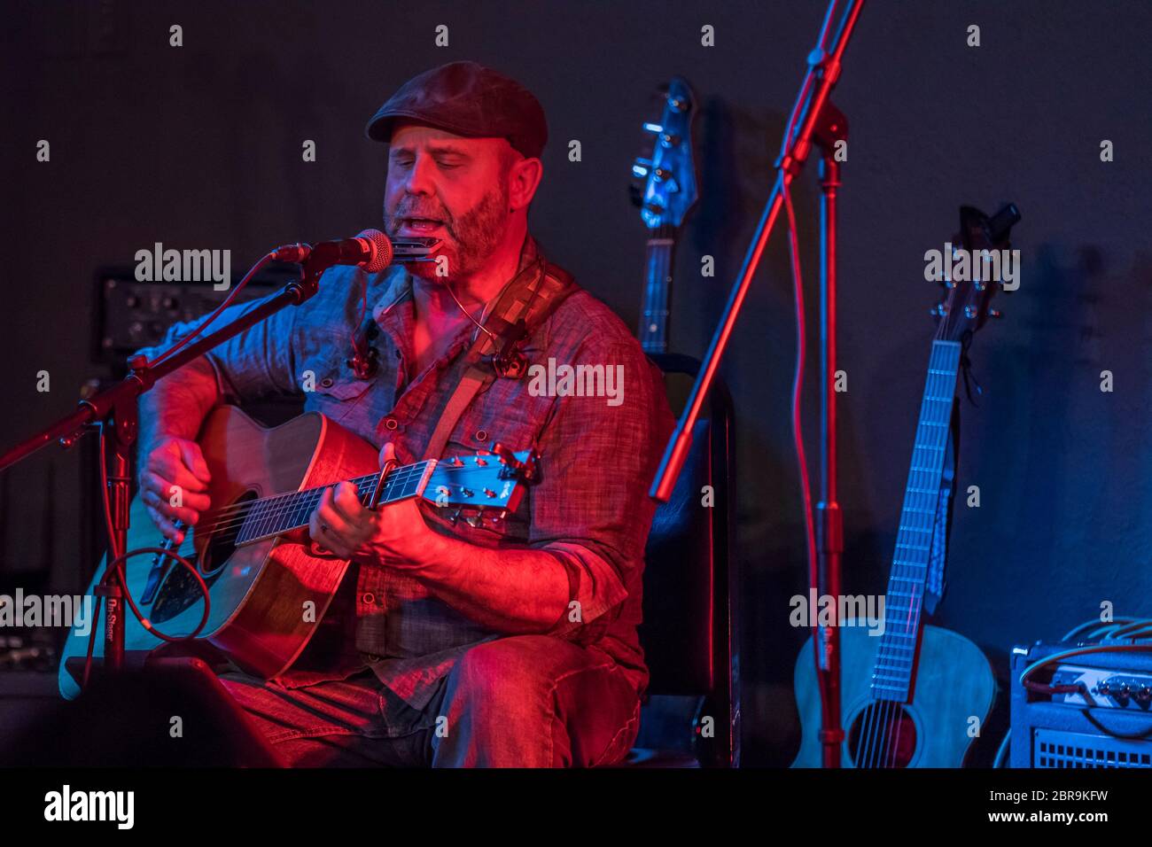 Male folk singer, sitting as he sings and plays guitar, in indoor ...