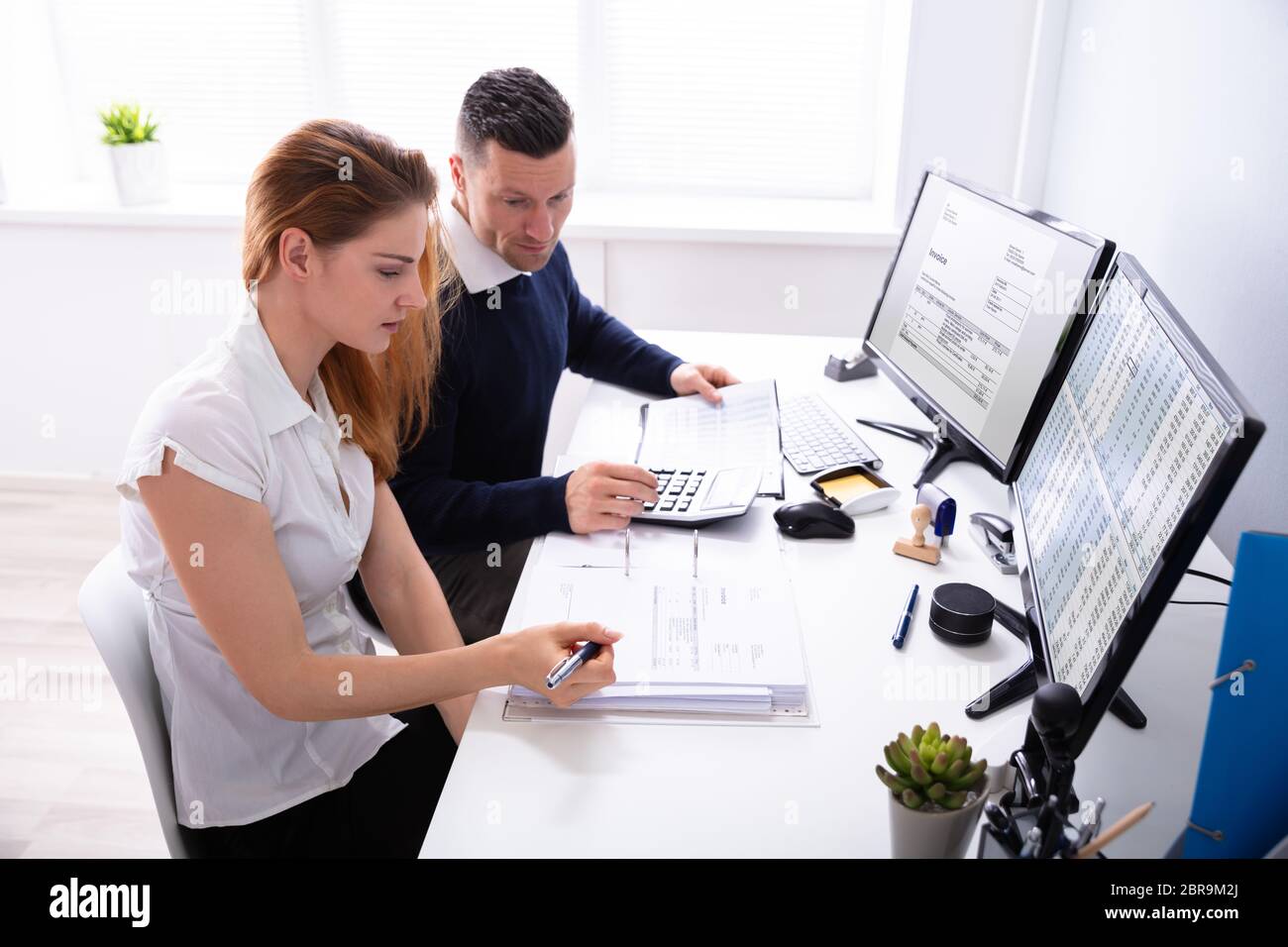 Side View Of Two Businesspeople Calculating Invoice With Calculator On ...