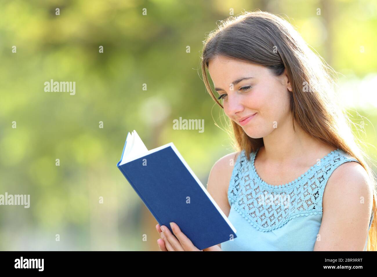 Serious woman reading a blank paper book on green background in a park ...
