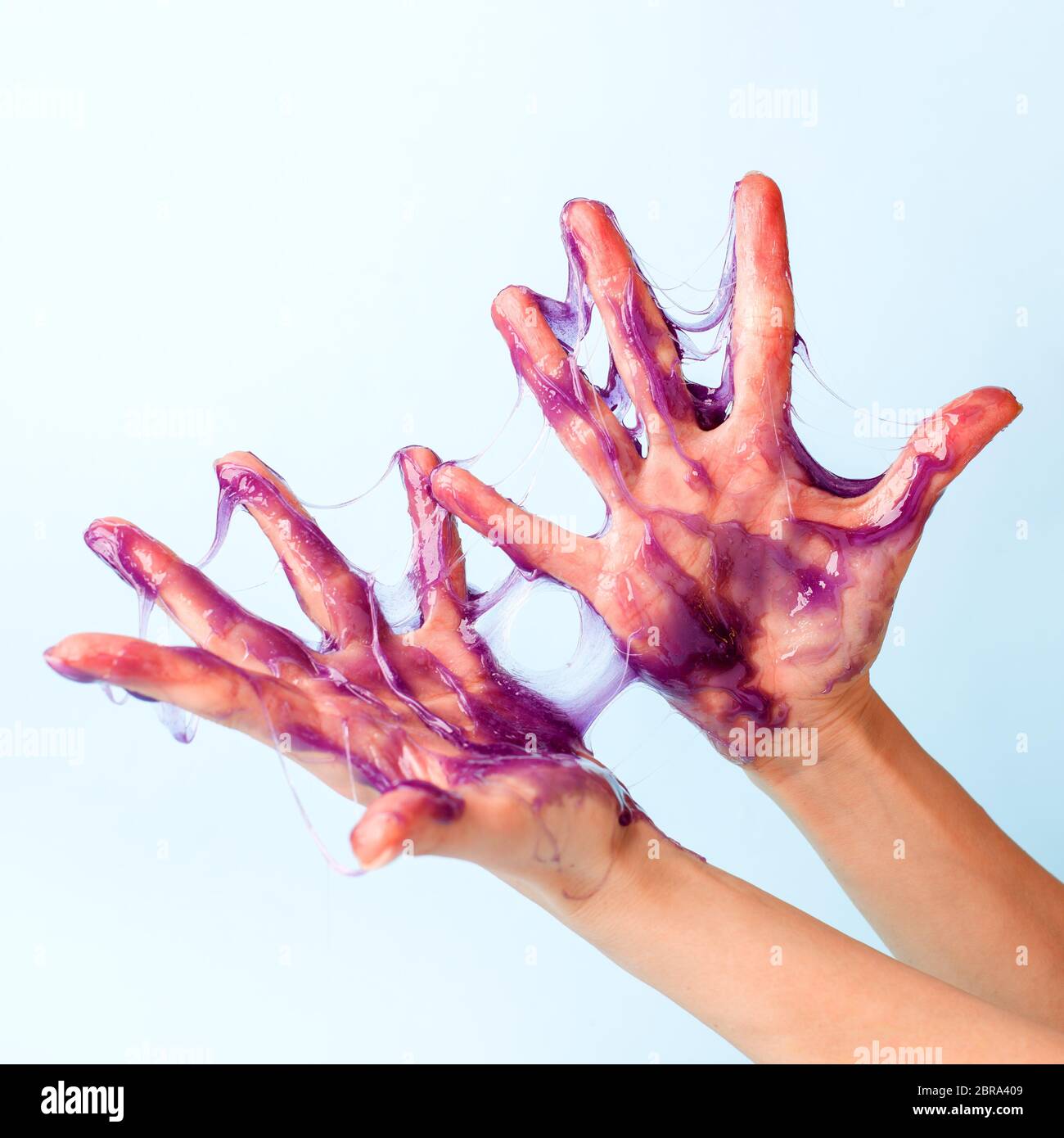 Young girl hands with sticky purple slime on blue background, liquid ...