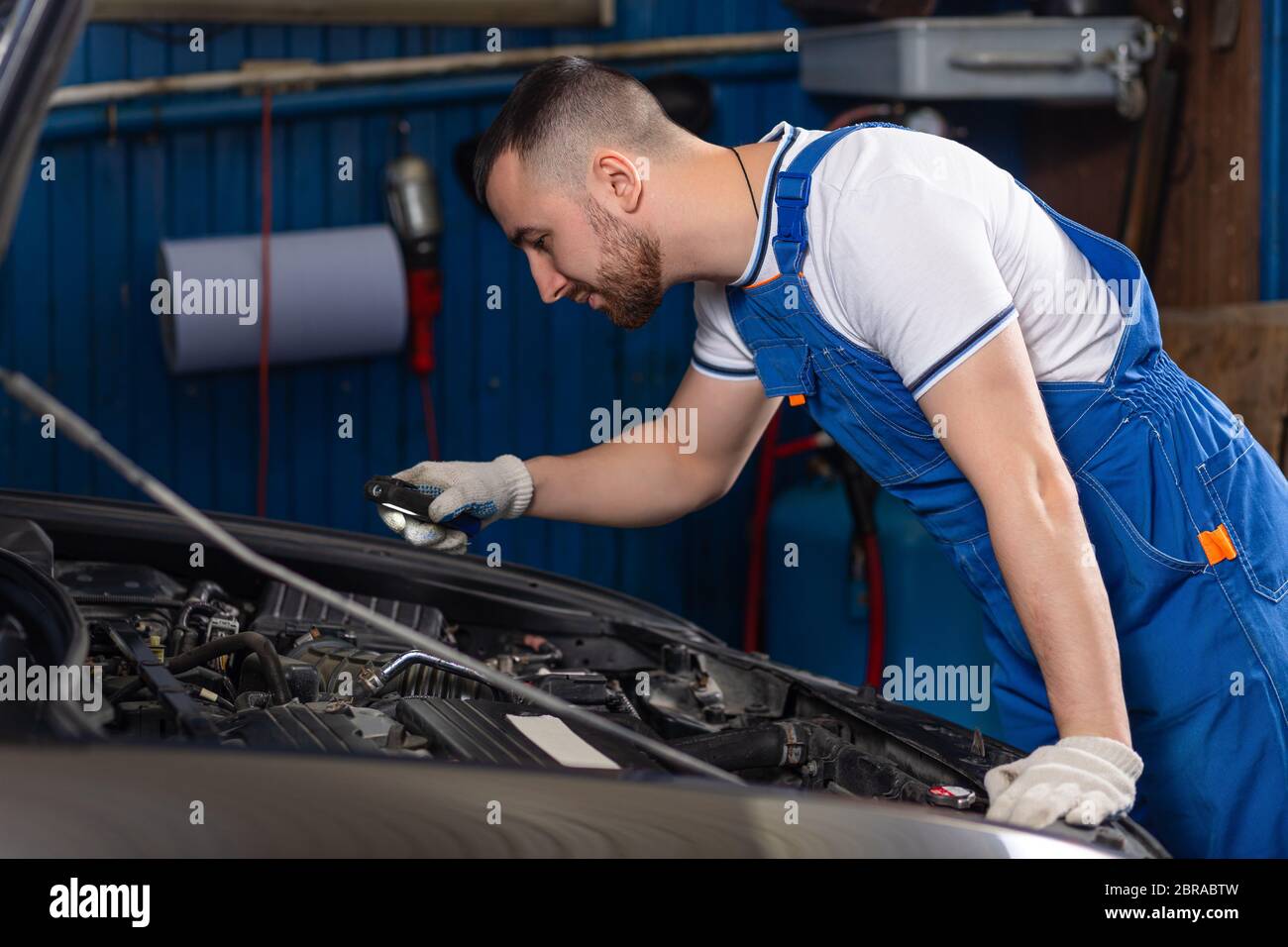 Handsome young male auto mechanic in special uniform clothes holding a ...