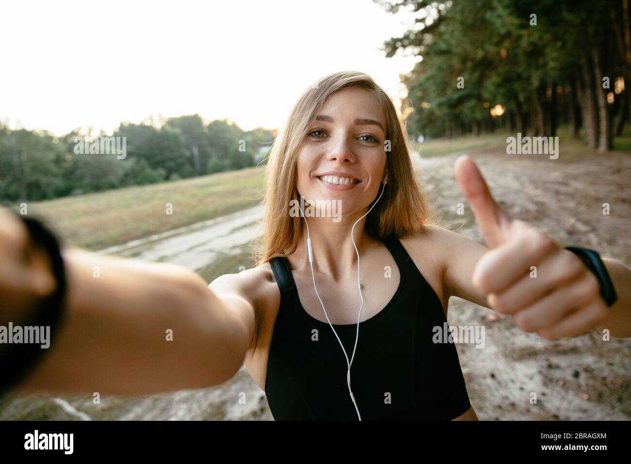 Smiling Beautiful Girl In Sportswear Taking A Selfie Showing A Big Finger Looking At Camera