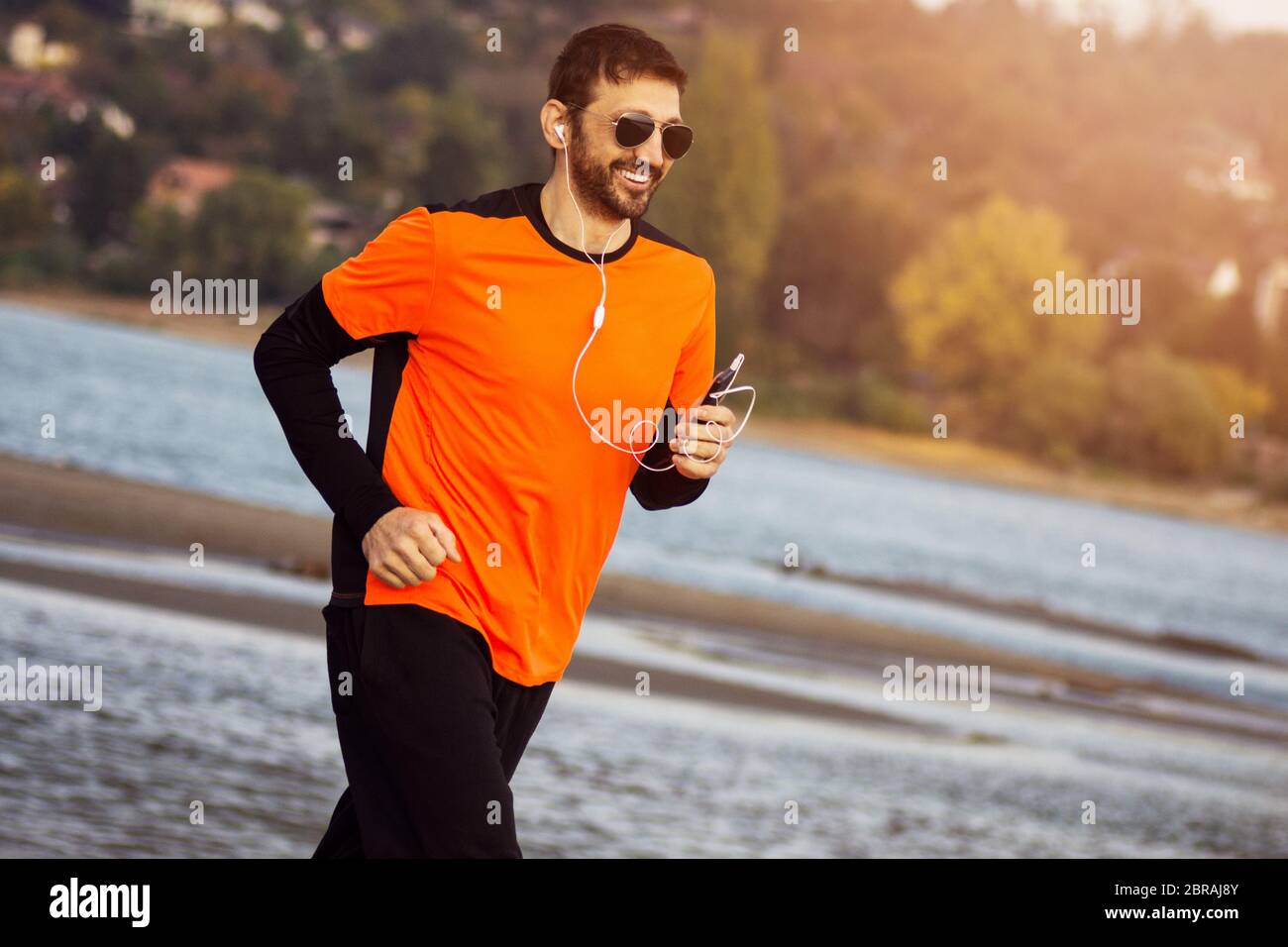 The smiling guy in orange sports clothing with earphones and sunglasses ...