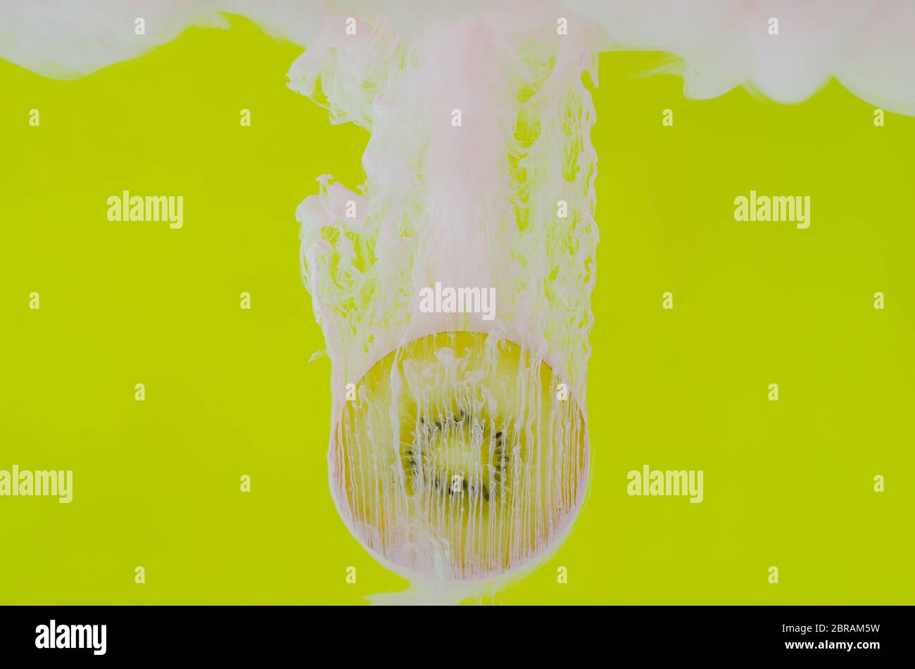 Blurred focus of dissolving pink poster color in water with slice kiwi ...