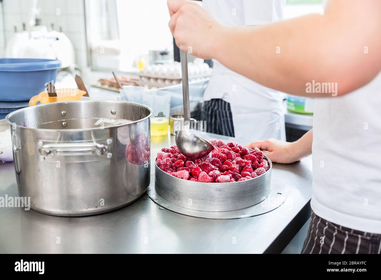 Woman in confectioner bakery working on fruit cake putting raspberries ...