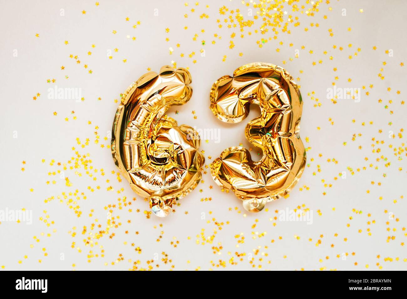 small foil gold balloons numbers 63 inflated with helium on a beige ...