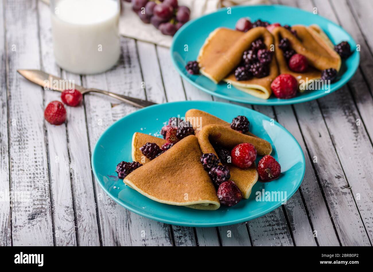 Homemade crepes with frozen berries, topped sugar, rustic wood board ...