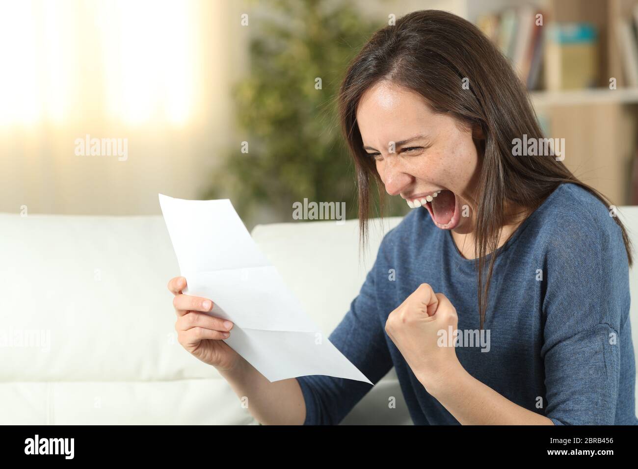 Excited woman reading a letter sitting on a couch in the living room at ...
