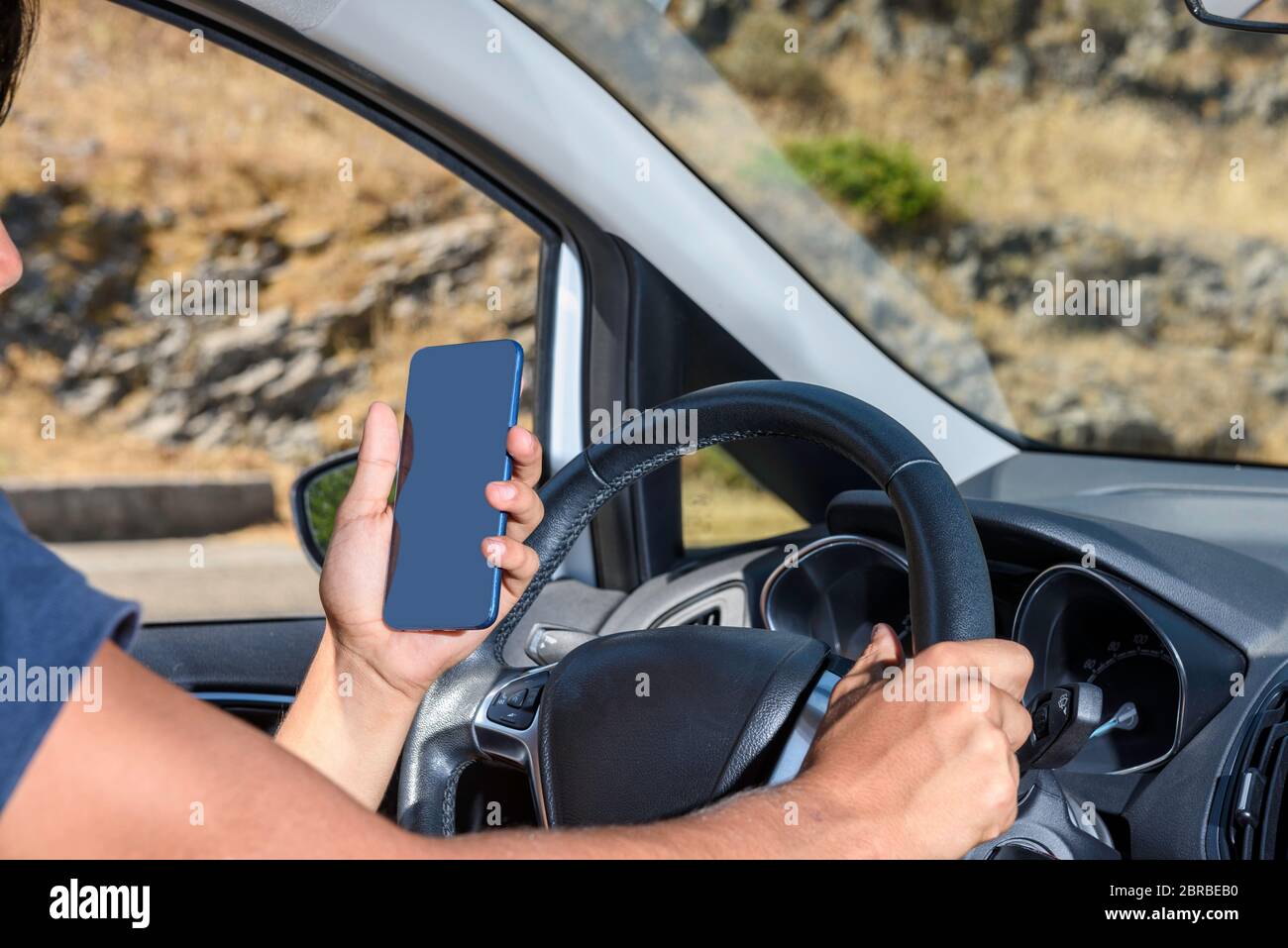 Young driver, using smartphone, on the road in the car. Distraction and ...