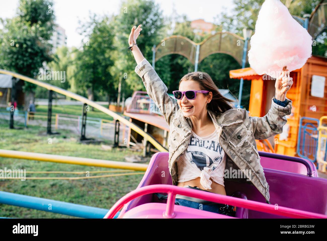 Attractive cheerful girl in sunglasses riding a roller coaster, having ...