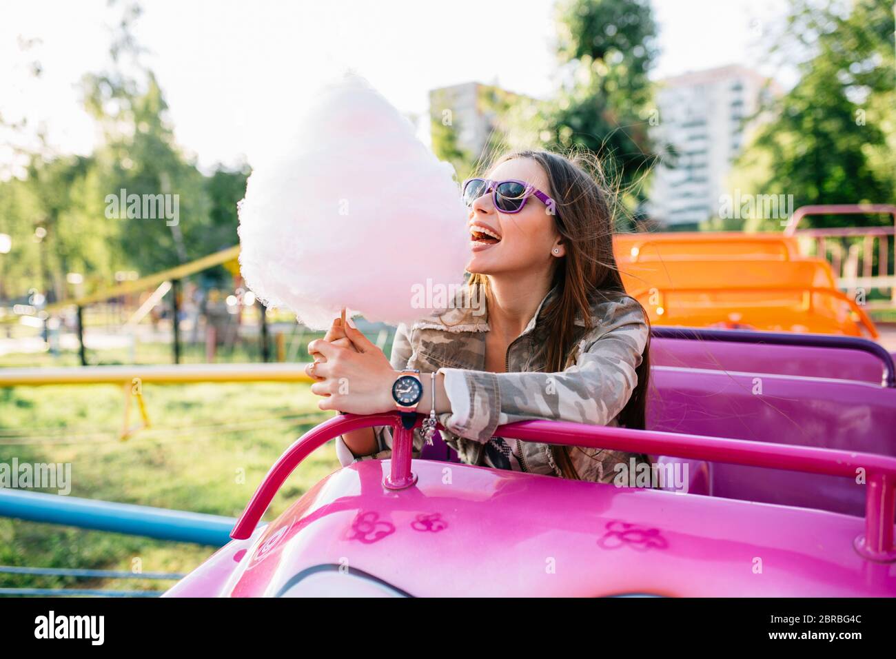 Cheerful beautiful woman eating a cotton candy, while riding a roller ...