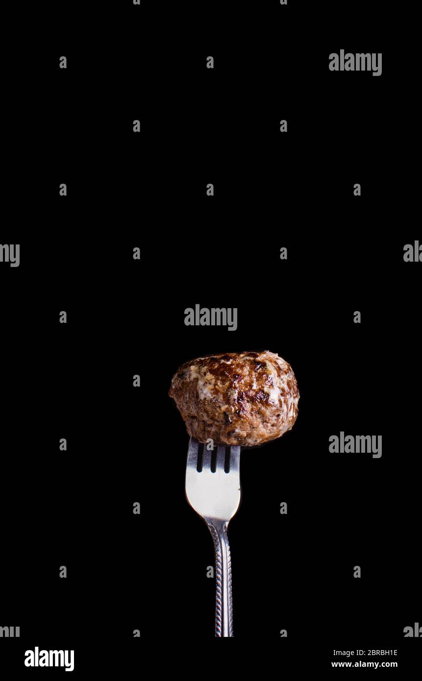 Meatball on black background on fork, place for your advertisment, text ...