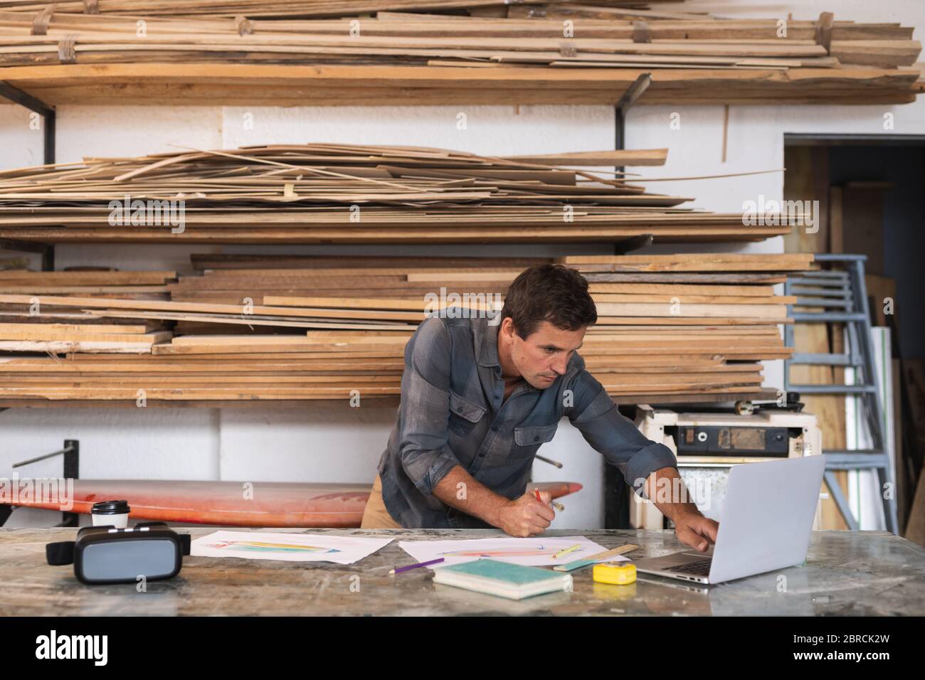 Caucasian male surfboard maker standing behind the counter and using ...