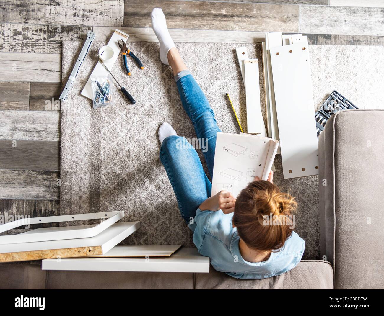 Concentrated young woman reading the instructions to assemble furniture ...