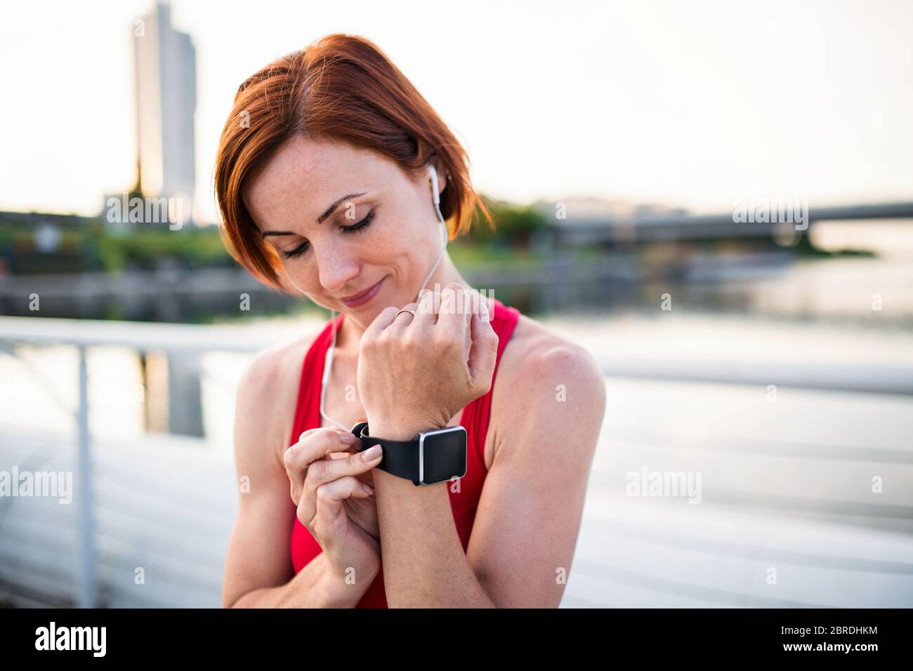 Young woman runner with earphones in city, using smartwatch Stock Photo ...