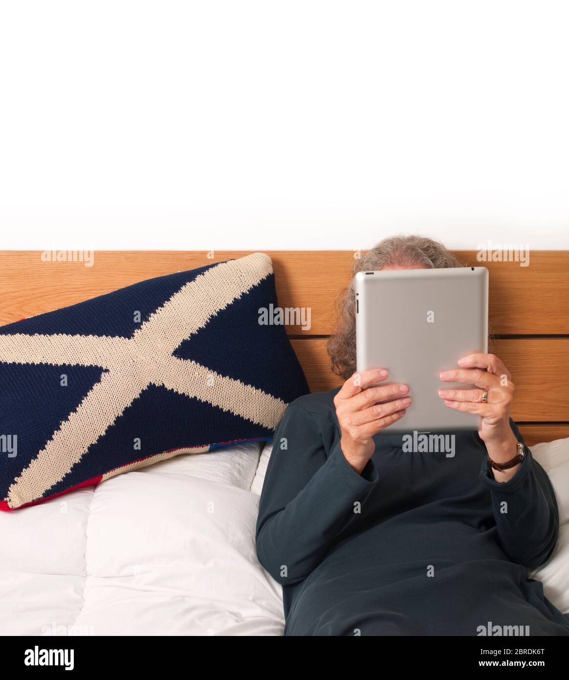 Older woman lying on a bed browsing the internet with a digital tablet ...