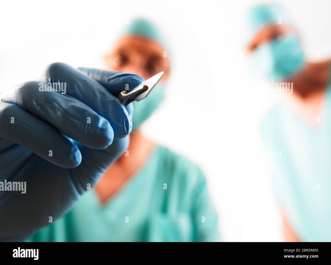 Surgeon in operating theatre with scalpel watched by other medic ...