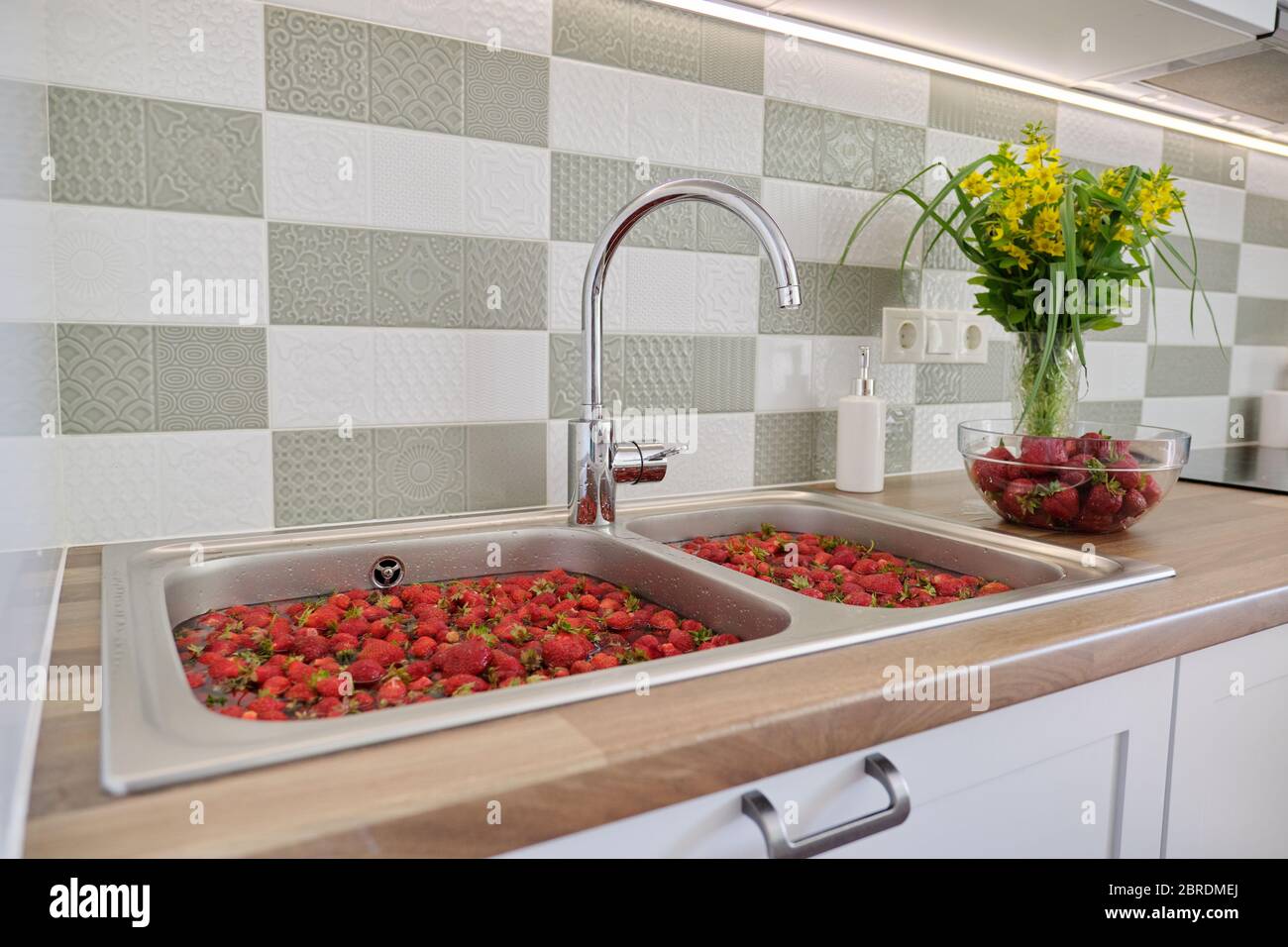 Strawberry season, washing berries in water in wash basin at home ...