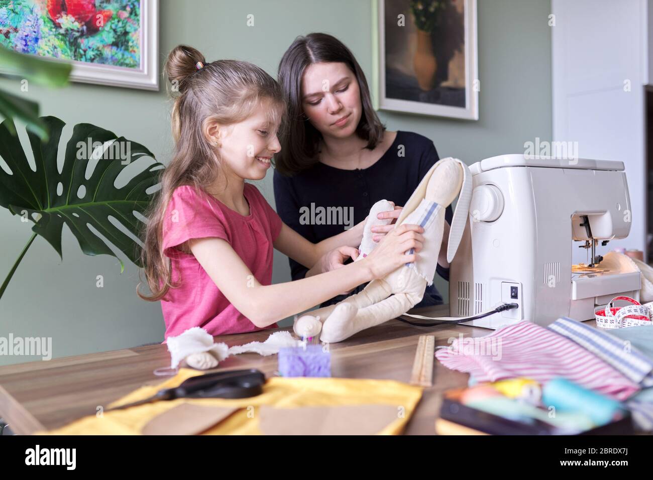 Family, two girls sisters teenager and younger together sewing toy doll ...