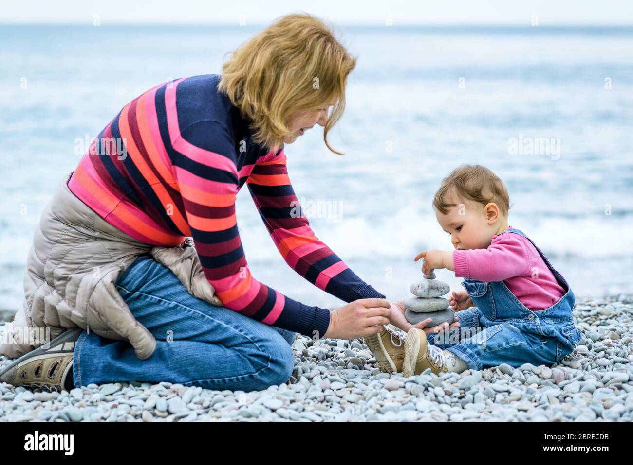 Mother and her baby playing with pebbles on the beach Stock Photo - Alamy