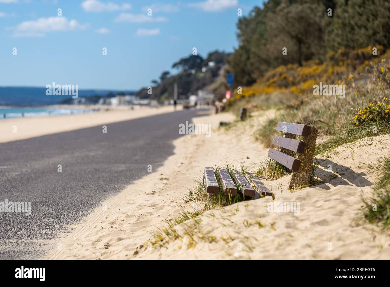 Public bench covered in sand on Poole beach promenade on sunny day ...