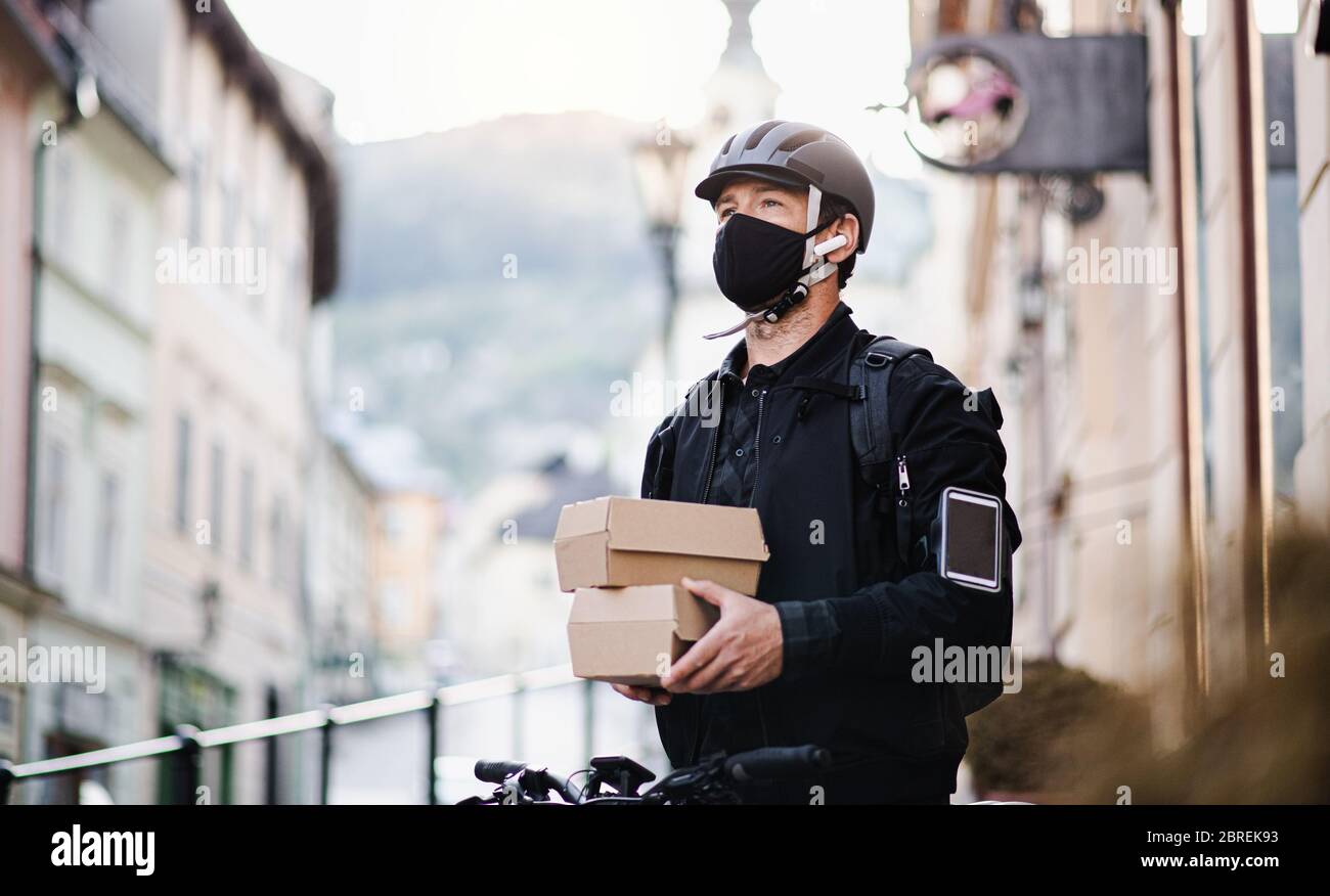 Delivery man courier with face mask and smartphone delivering parcel ...
