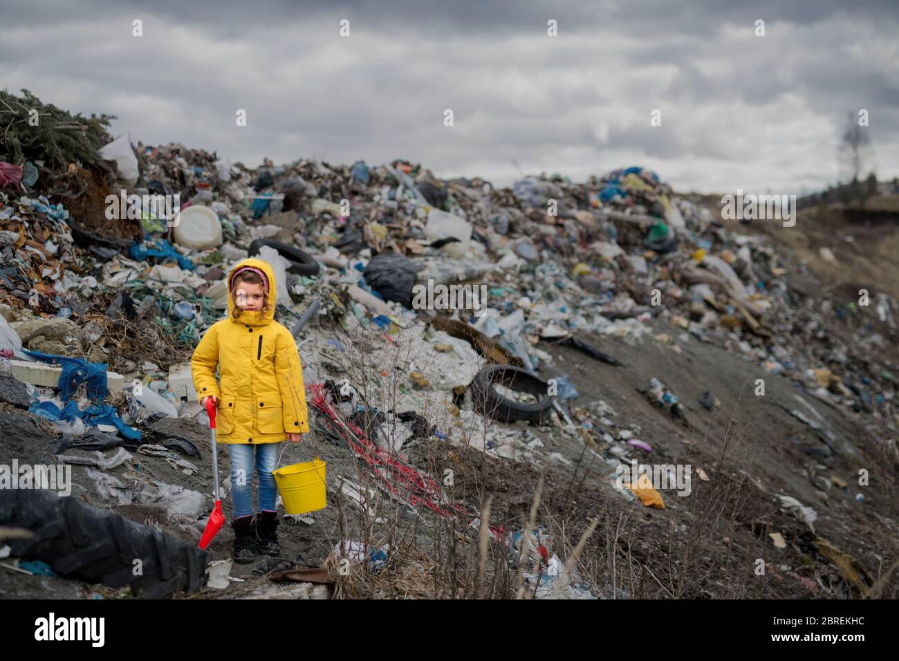 Front view of small child standing on landfill, environmental pollution ...
