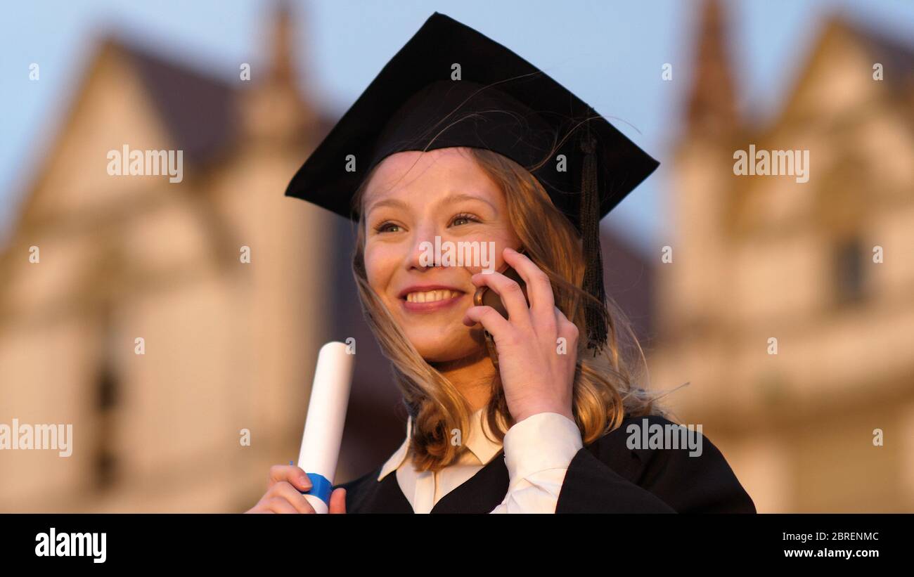 Happy pretty girl graduate in gown talking on mobile phone Stock Photo ...
