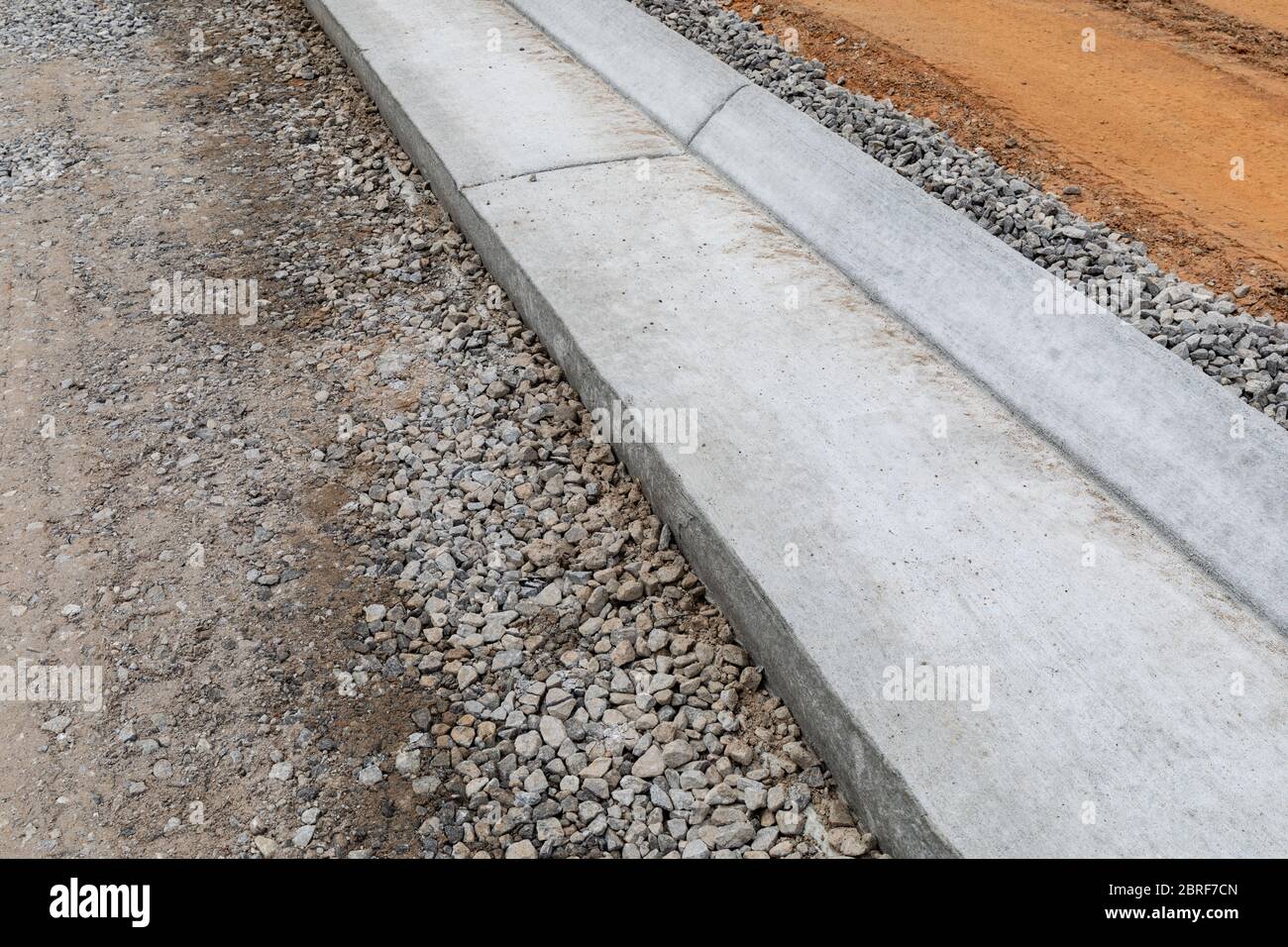 New extruded curb edging for street under construction, gravel road bed ...