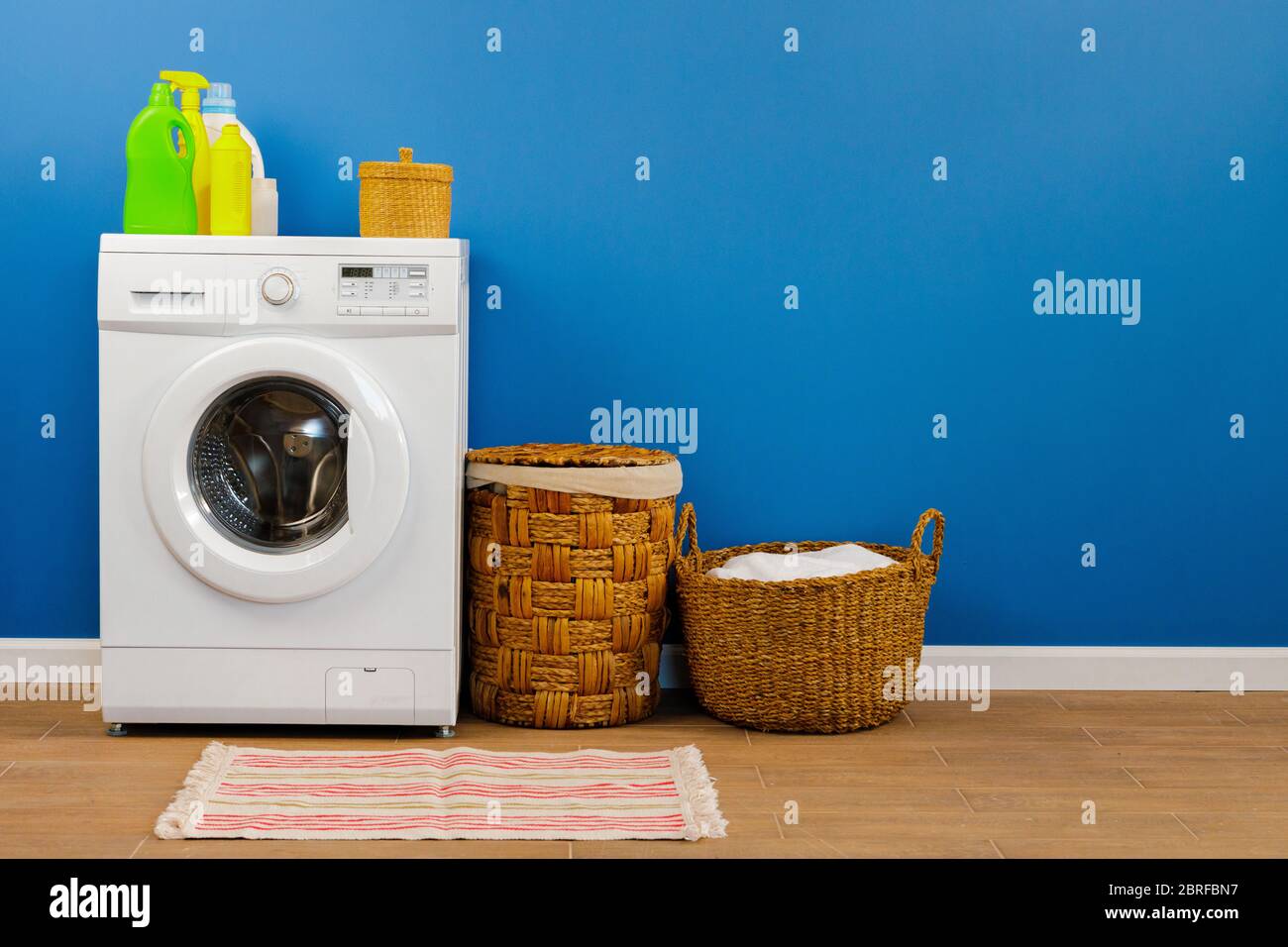 Washing machine with laundry on blue wall background Stock Photo - Alamy