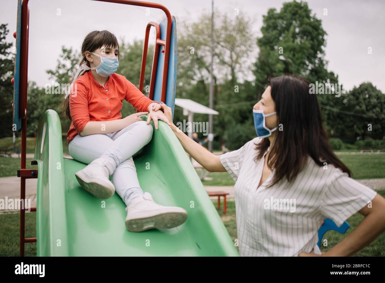 Side view of mother and daughter at the playground, wearing masks ...