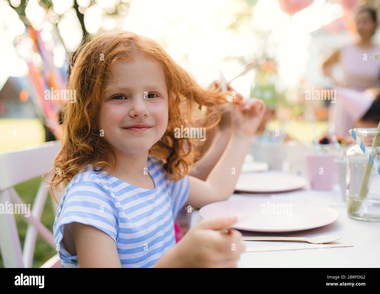 Small girl sitting outdoors in garden, birthday celebration concept ...