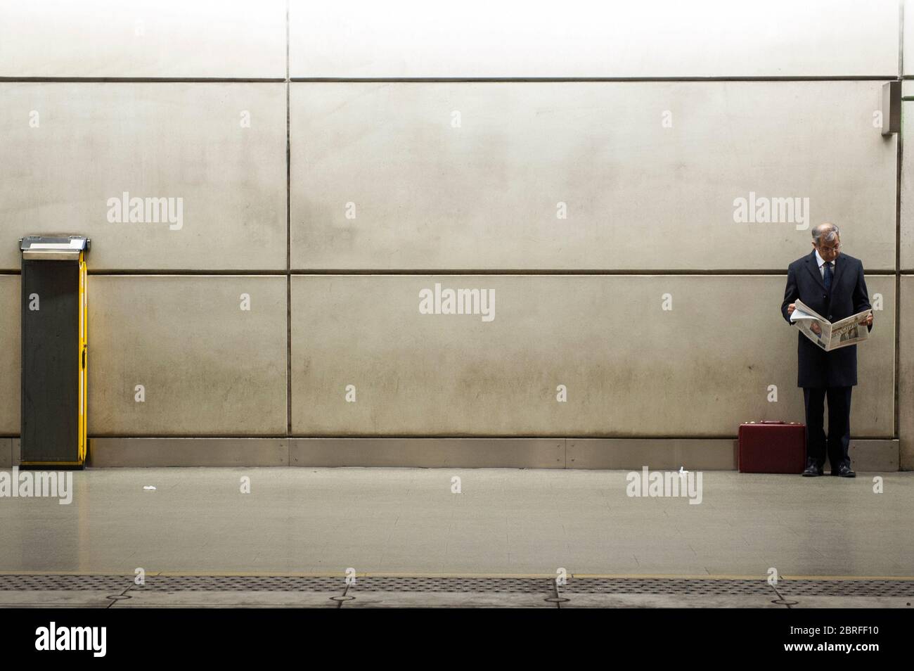 London City Office worker stands at the station reading a newspaper ...