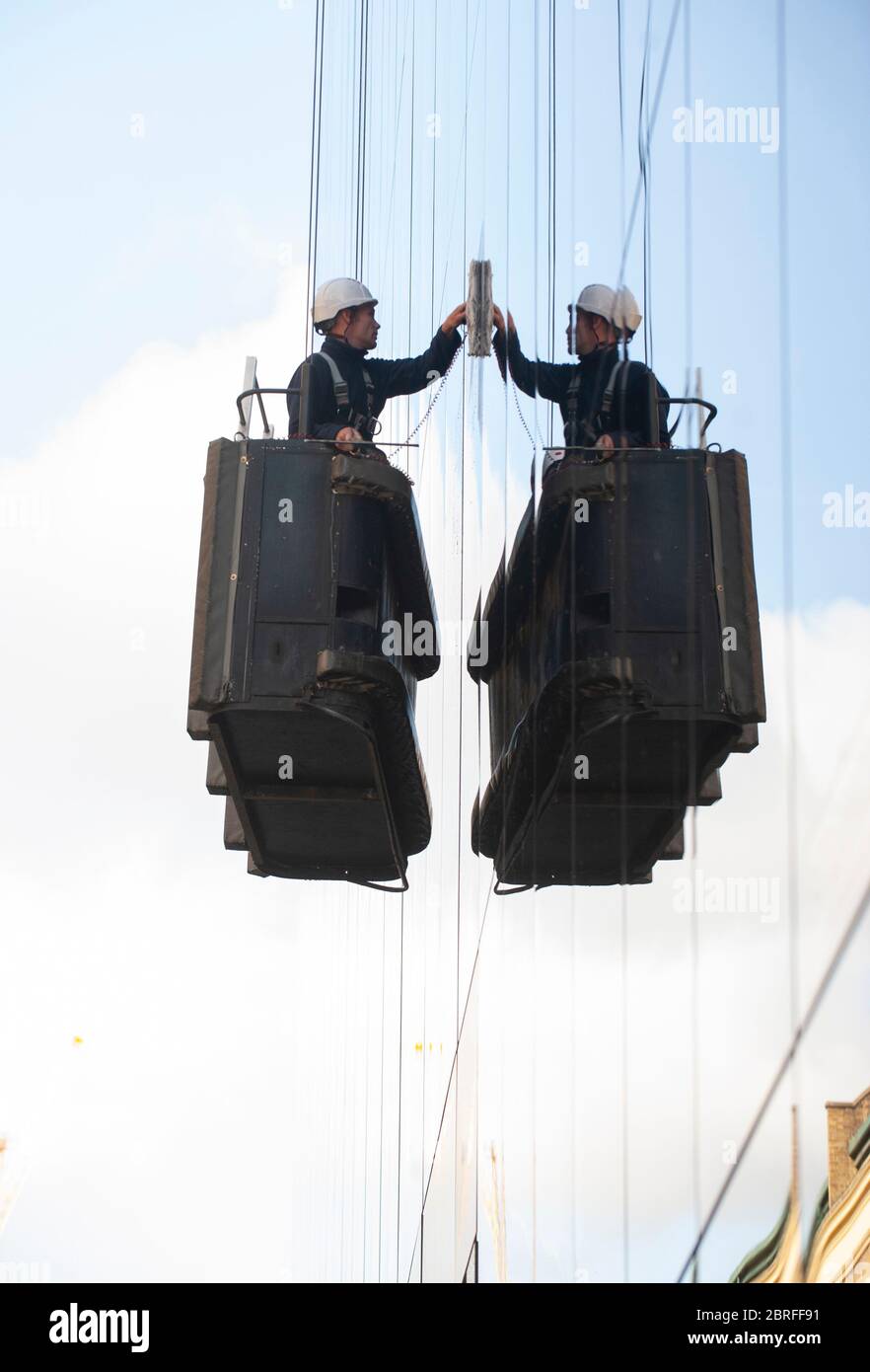 Two male window cleaners clean, and are reflected in, the outside glass ...