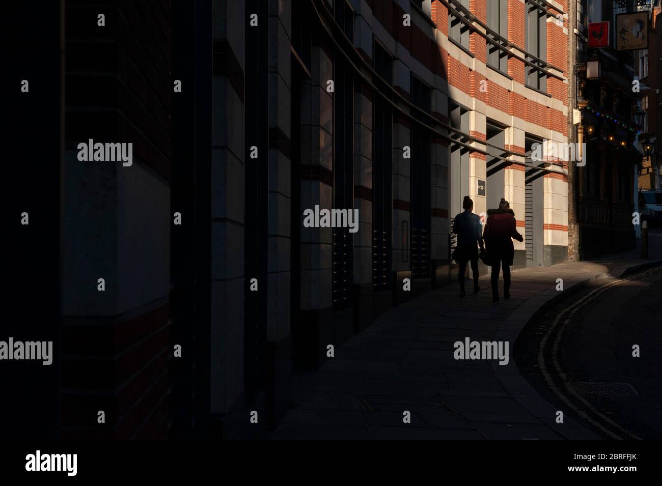 Two women walk along a curved street in the City of London with a shaft ...