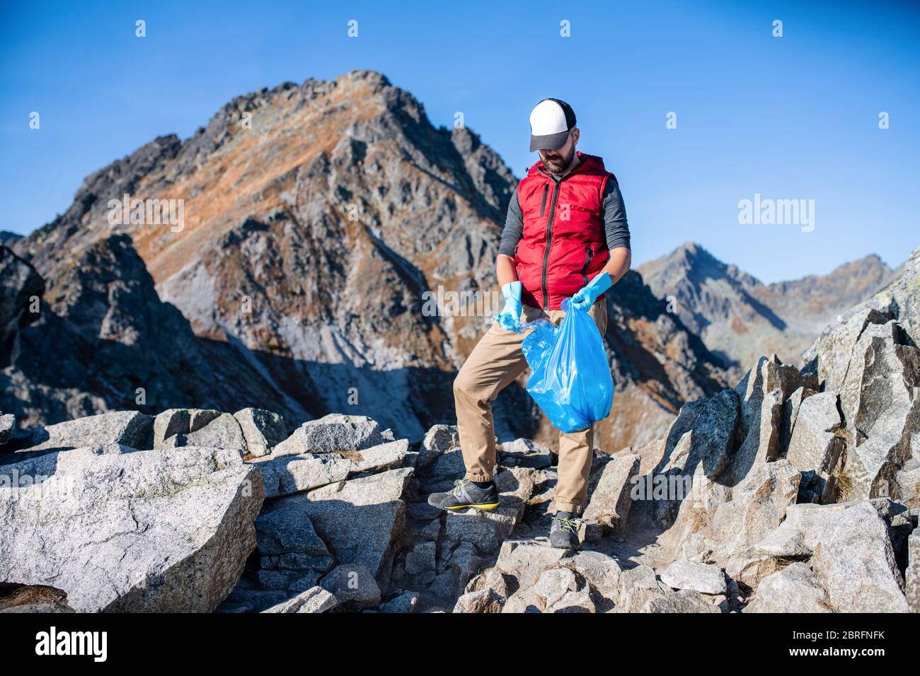 Man hiker picking up litter in nature in mountains, plogging concept ...