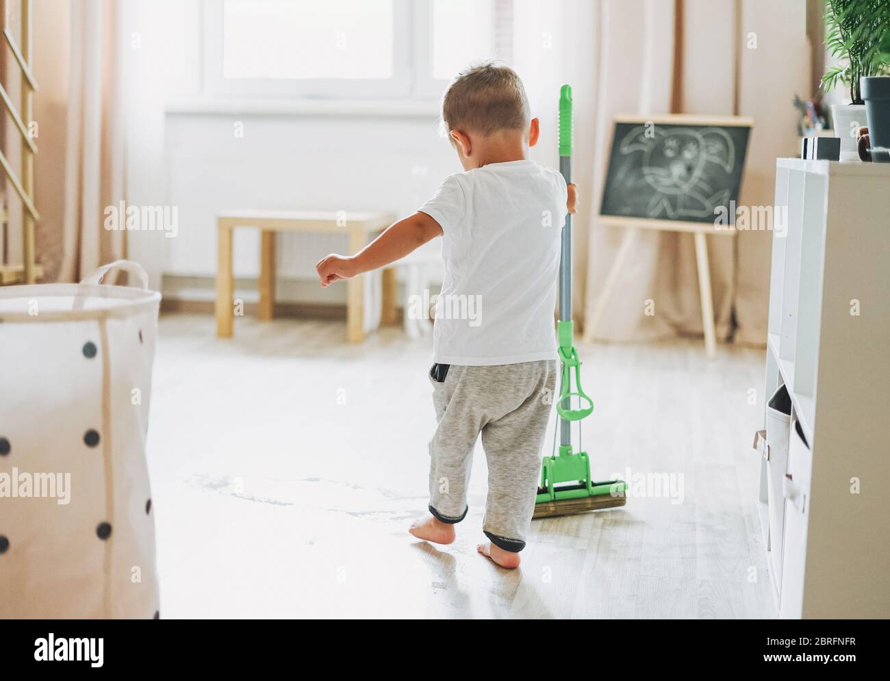 Cute baby boy with mop cleaning floor at room. Child wipes water in ...