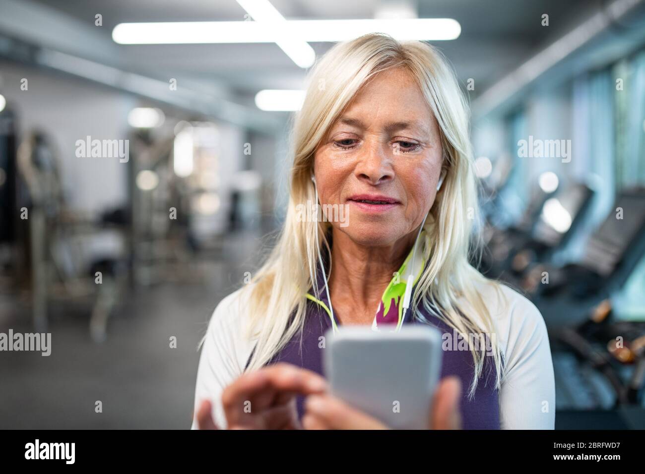 A senior woman with smartphone in gym resting after doing exercise ...