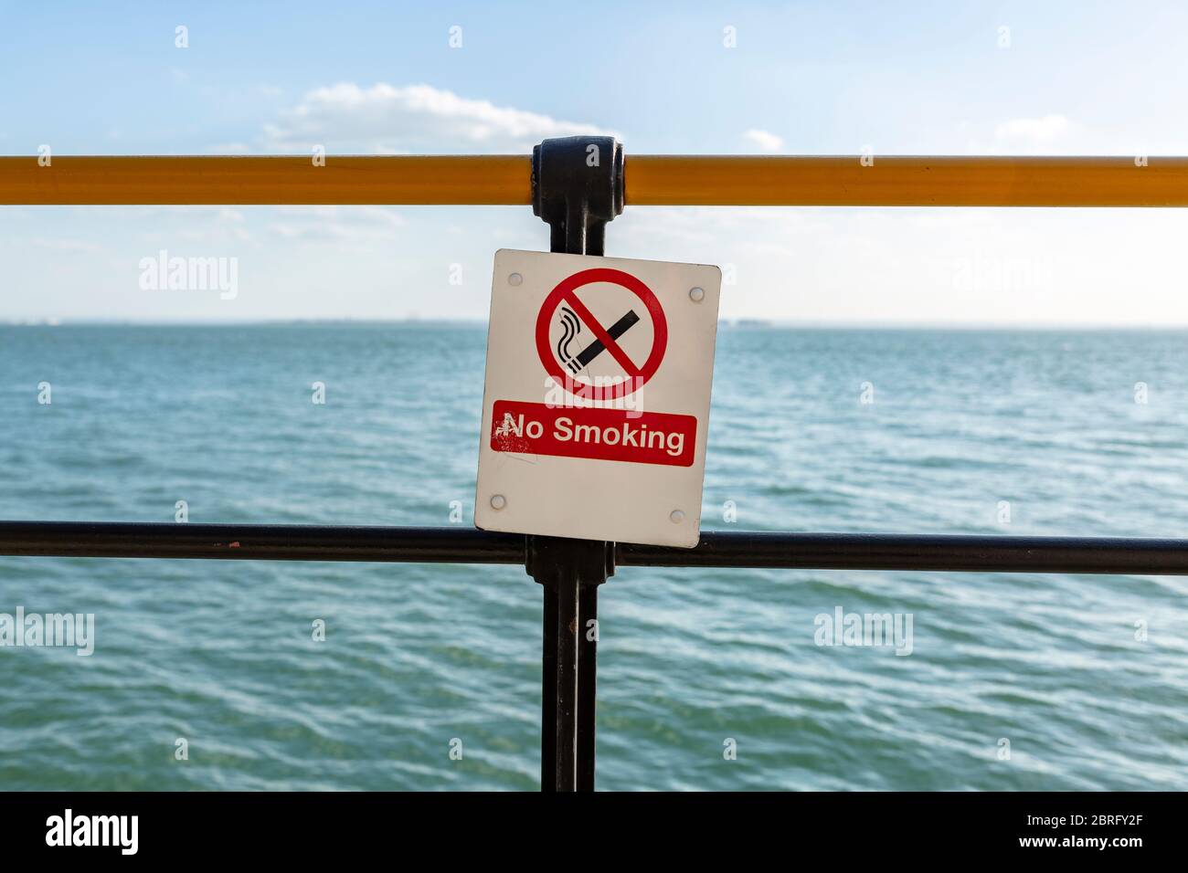 No Smoking Warning Sign attached to a fence in front ofa blue sea Stock ...