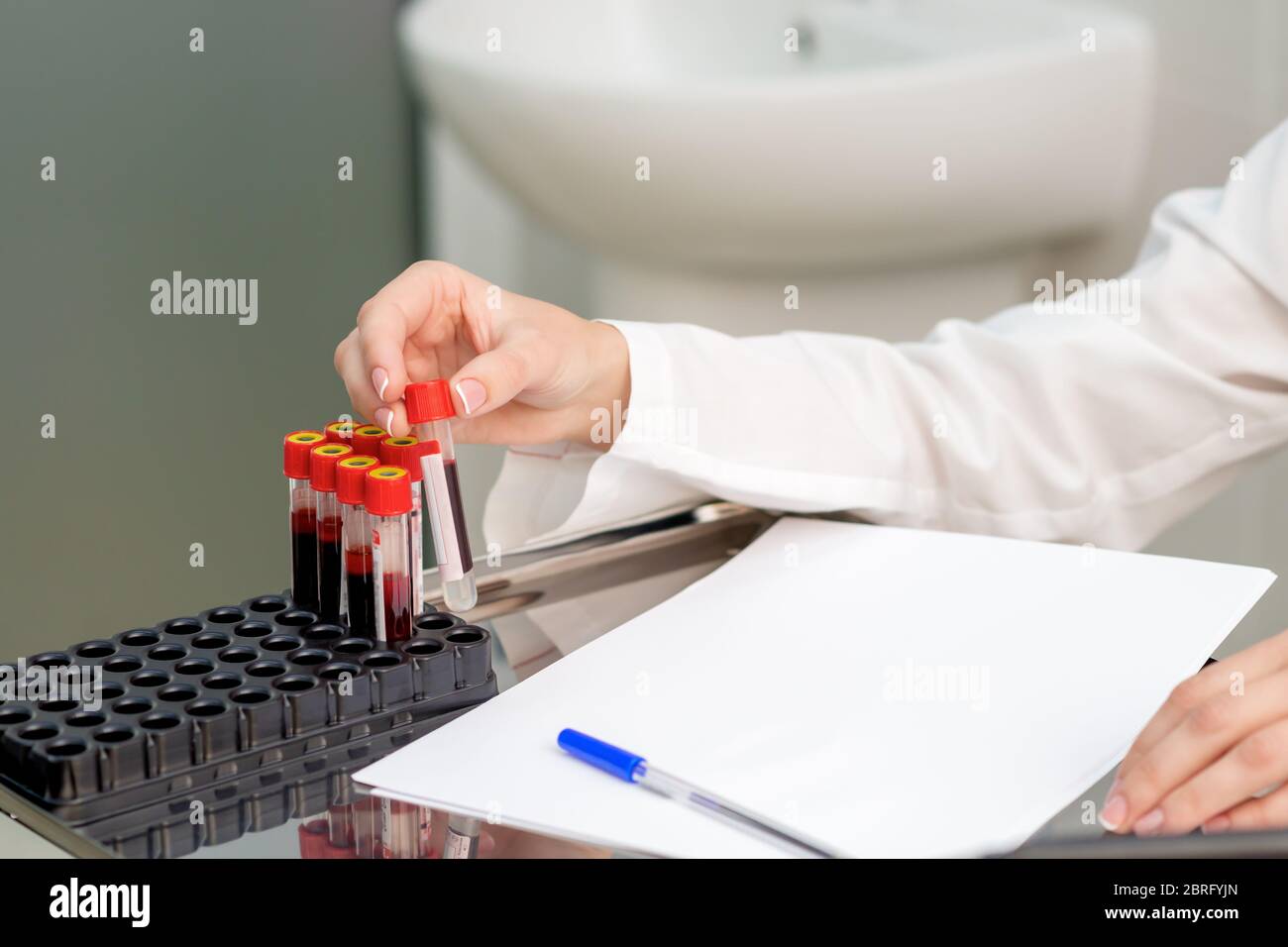 Hand of doctor is taking test tube with blood from tray on table in the ...