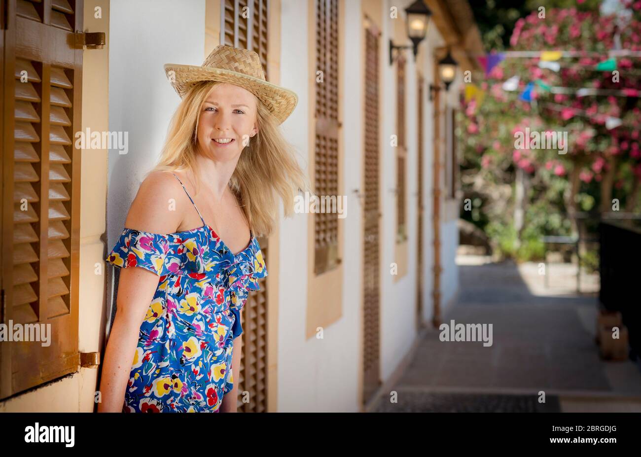 Pretty young woman wearing a colourful sundress and hat in a street in ...