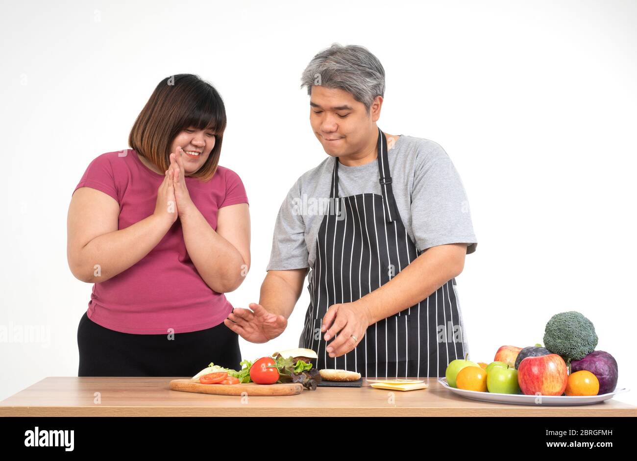 Happy overweight couple cooking a burger in the kitchen room. A ...
