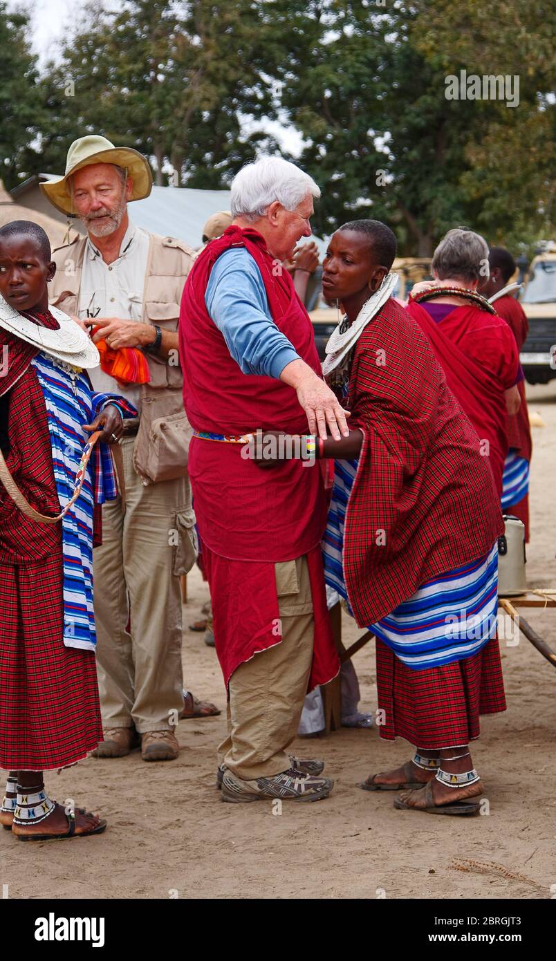 Maasai woman, wraps male visitor in tribal dress, arm moving, double ...