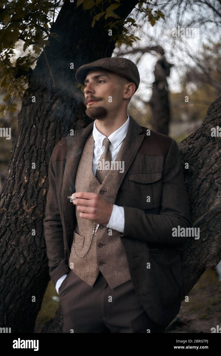 Retro 1920s portrait of an English gangster with a flat cap. Smokes a ...