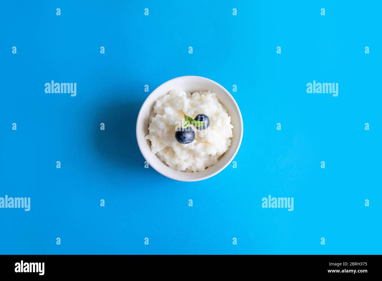 Tasty rice porridge with blueberry berries in a white bowl on blue ...