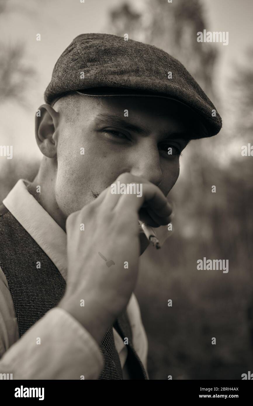 Retro 1920s portrait of an English gangster with a flat cap. Smokes a ...
