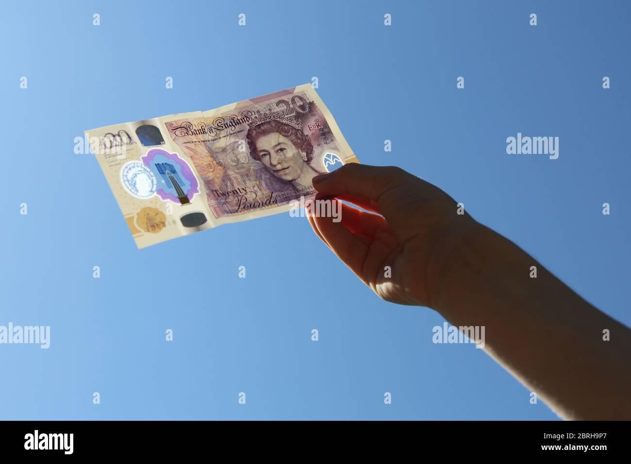 Hand holding a £20 note against blue sky, William Turner twenty pound ...