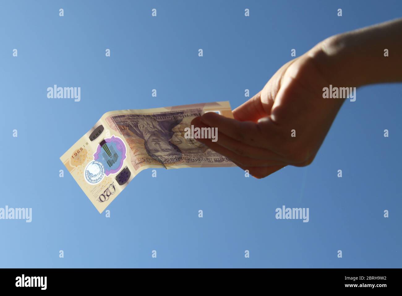 Hand holding a £20 note against blue sky, William Turner twenty pound ...
