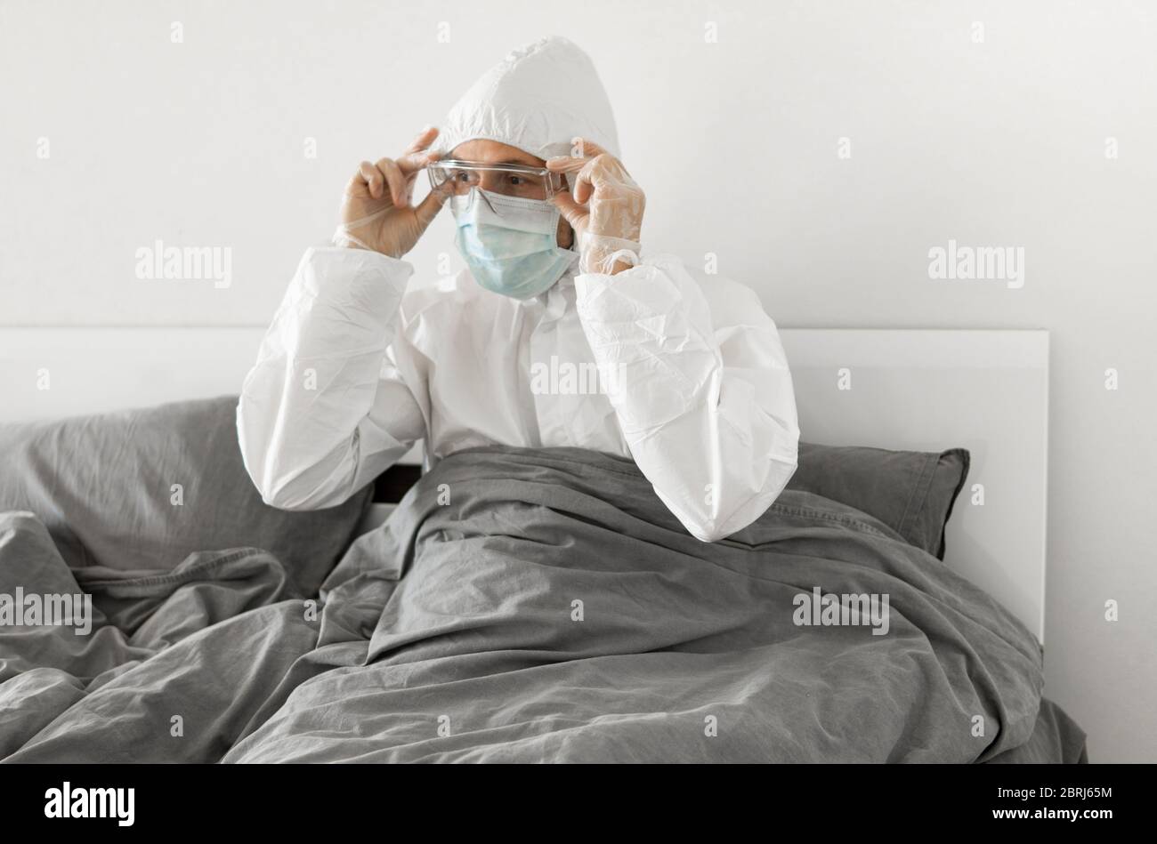 Portrait of man in protective white suit and face mask sitting in his ...