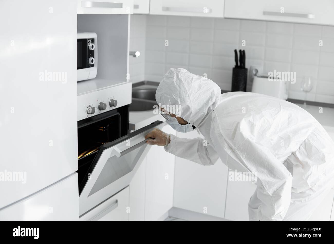 Man in white protective suit and in face medical mask cooks in the oven ...